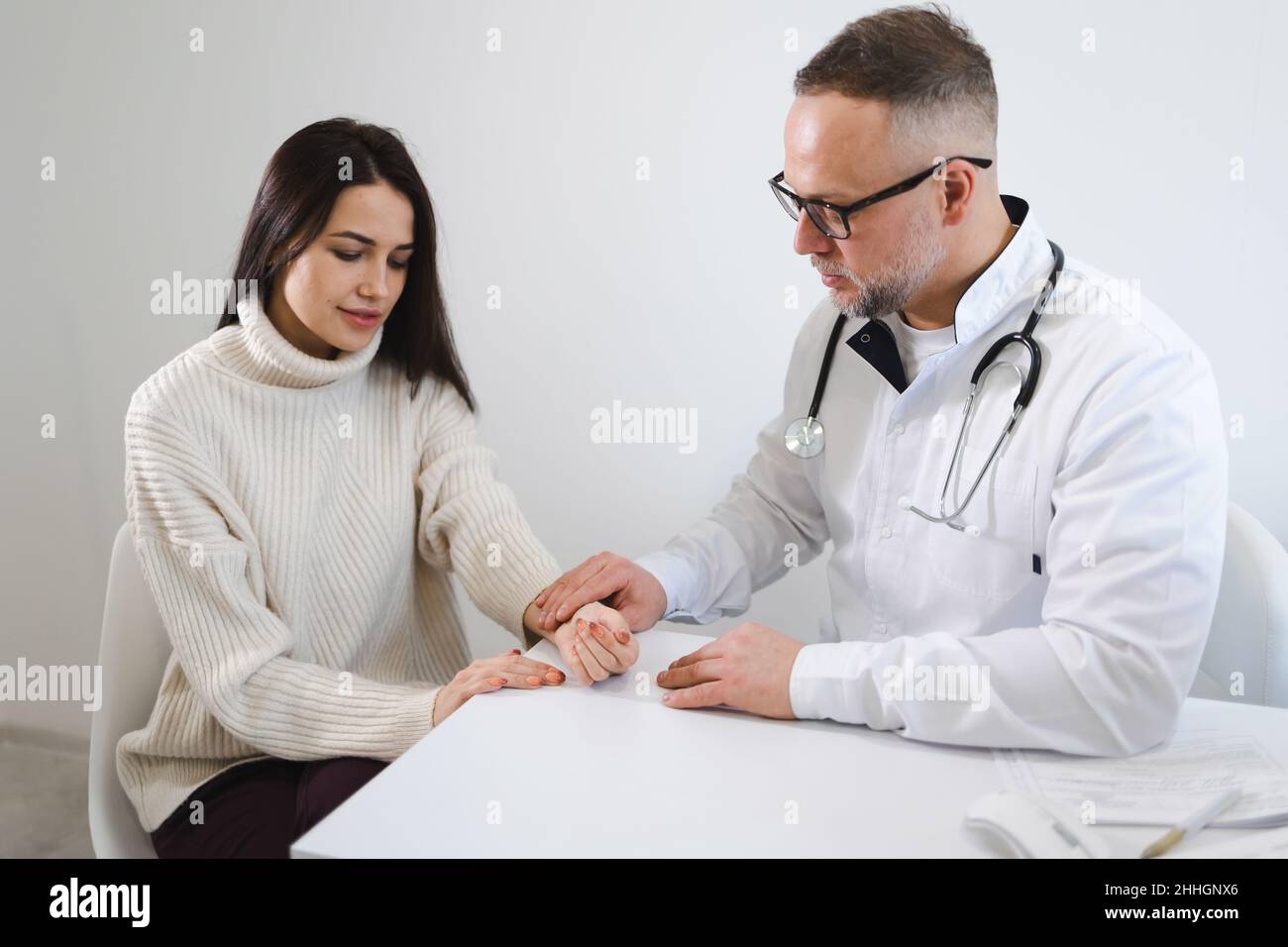 Male doctor measuring pulse of young female patient in clinic. Woman on ...