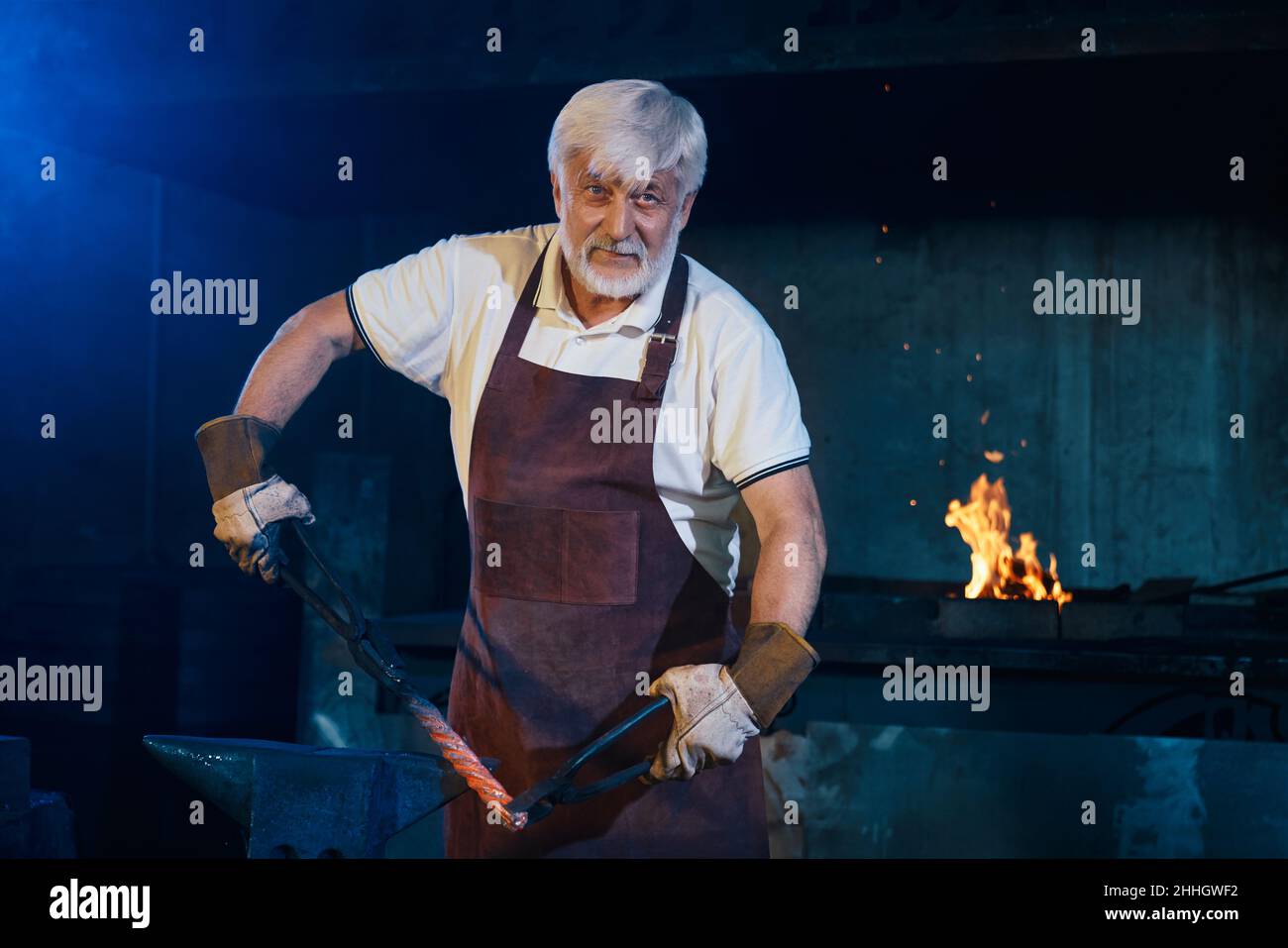 Caucasian aged blacksmith using industrial forceps for shaping molten ...