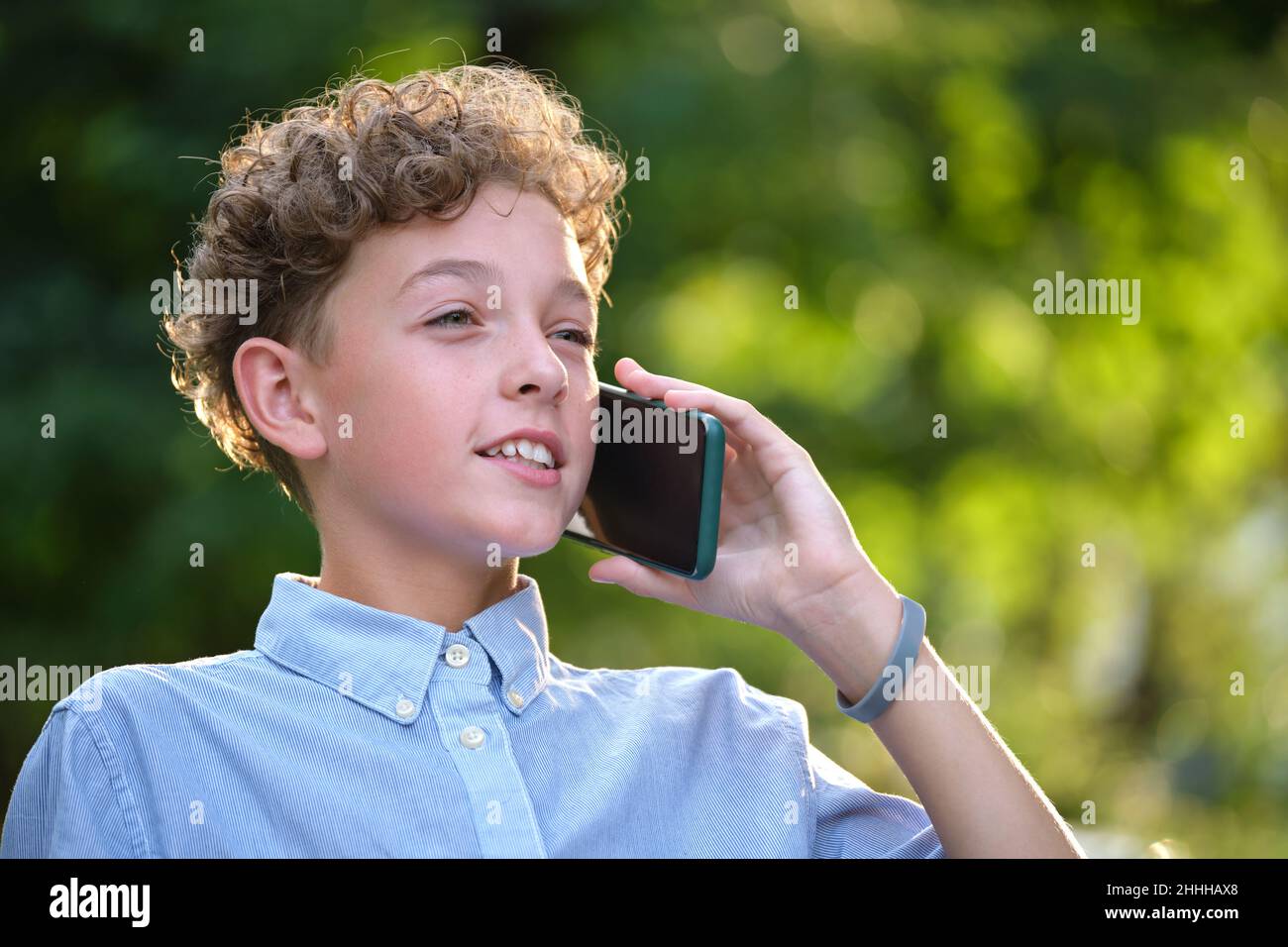 Happy young teenage boy talking on mobile phone outdoors in summer park ...