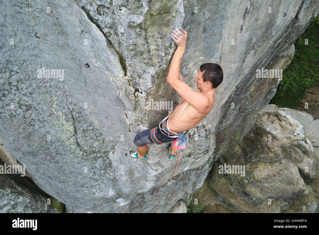 Young man climbing steep wall of rocky mountain. Male climber overcomes ...