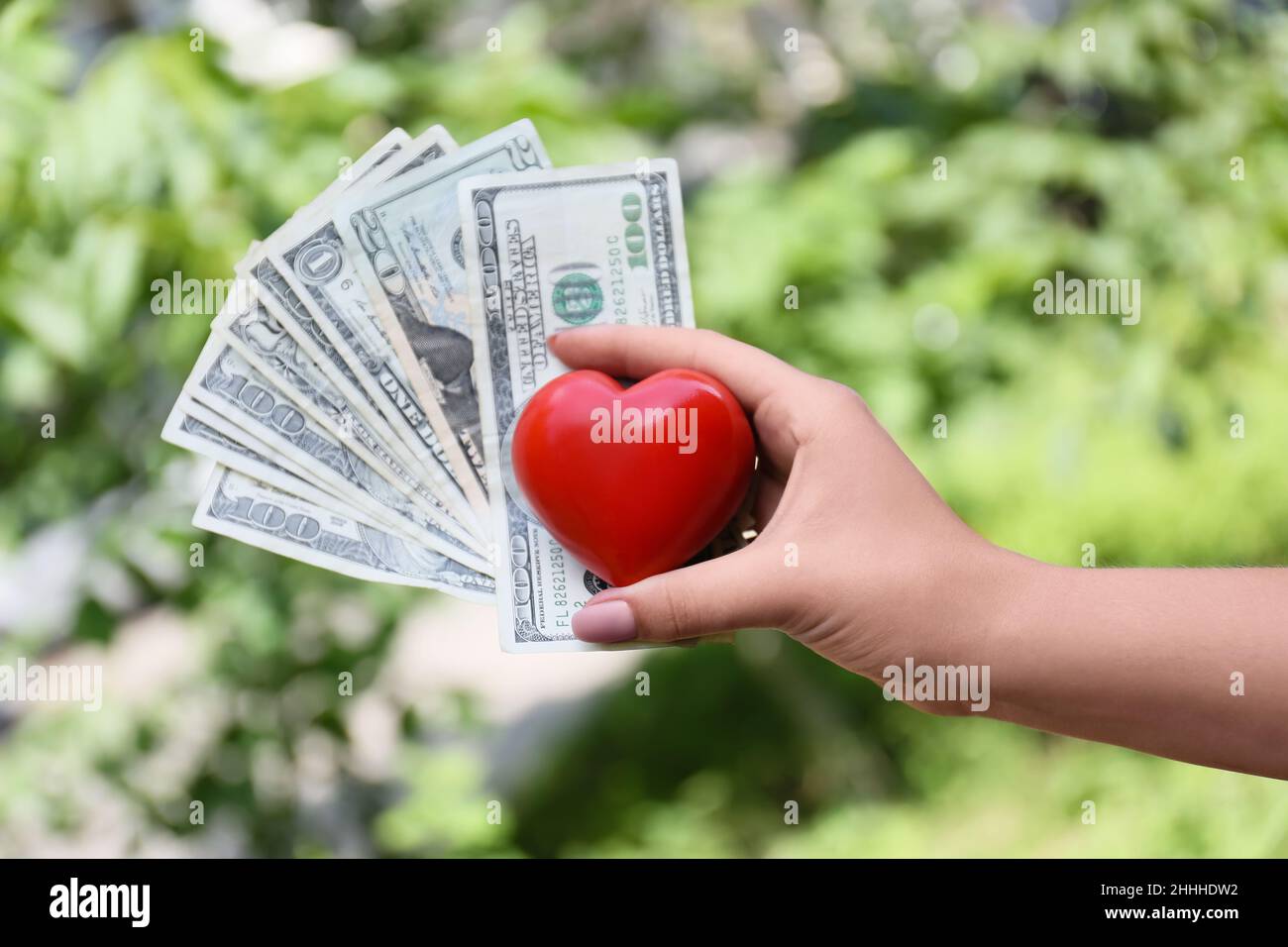 Female hand with red heart and money outdoors, closeup. Donation ...