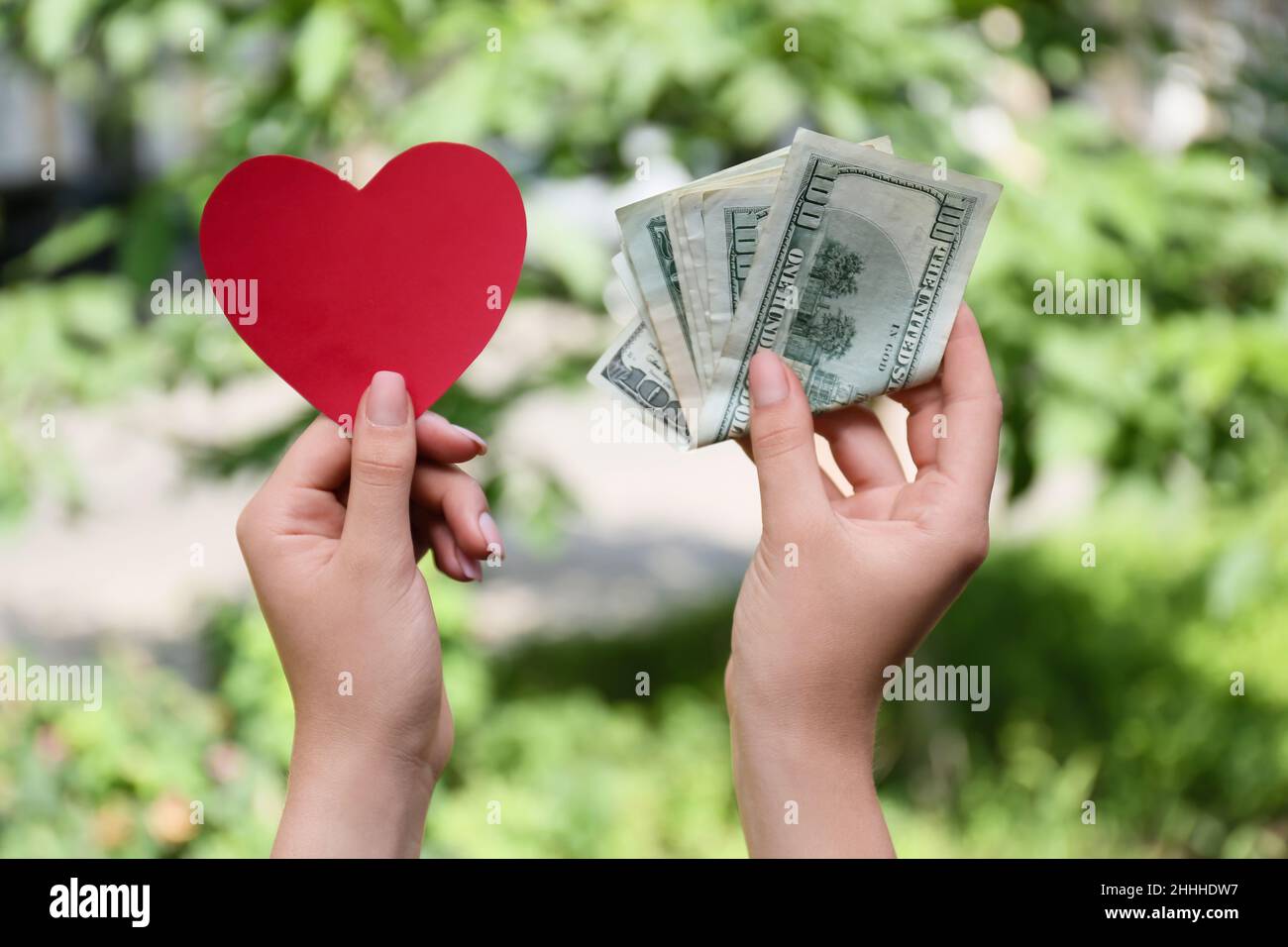 Woman holding red paper heart and money outdoors, closeup. Donation ...