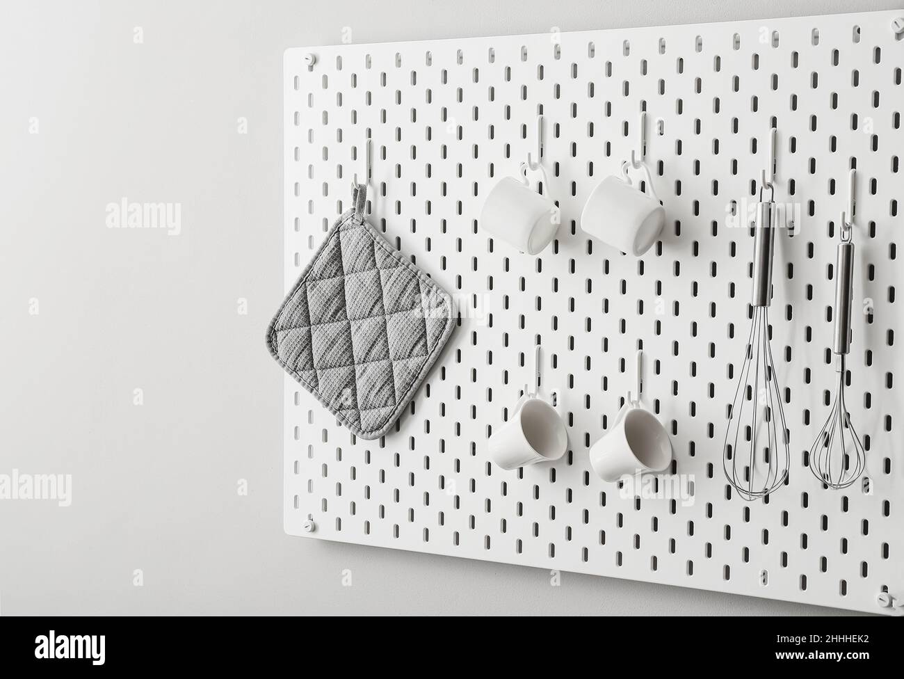 Pegboard with towel, cups and whisks on light wall Stock Photo - Alamy