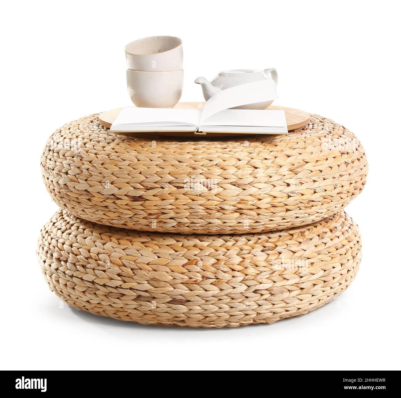 Opened book, cups and teapot on wicker poufs against white background ...