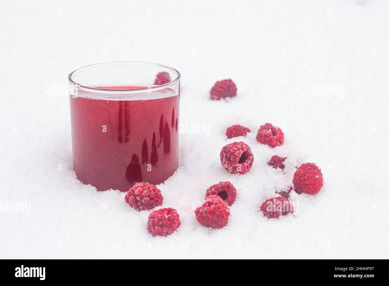 Frozen raspberries and raspberry juice in a glass in the snow. Healthy ...