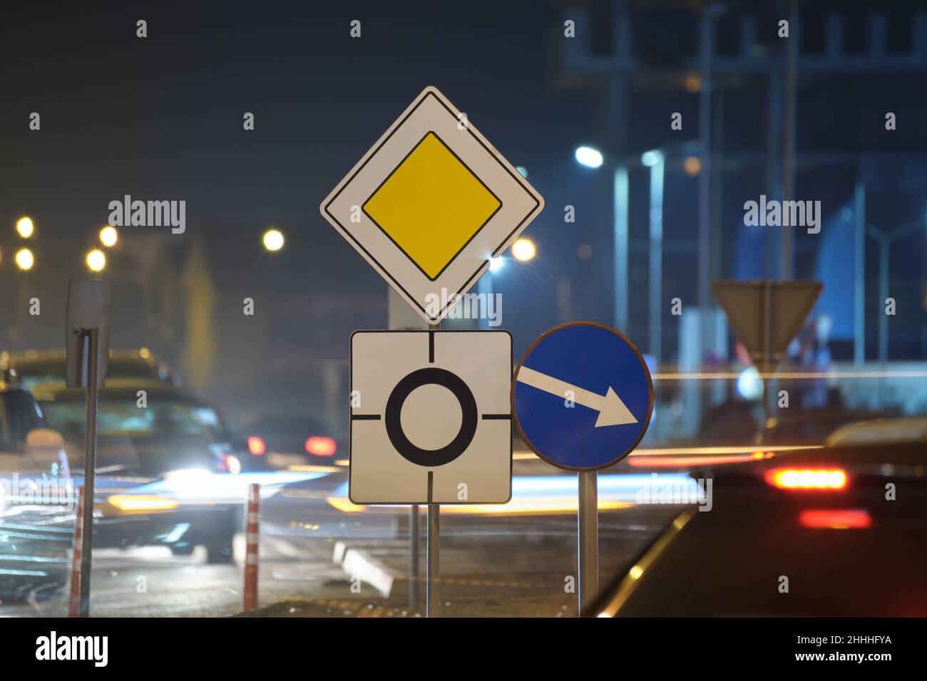 Roundabout road signs with blurred cars on city street traffic at night ...