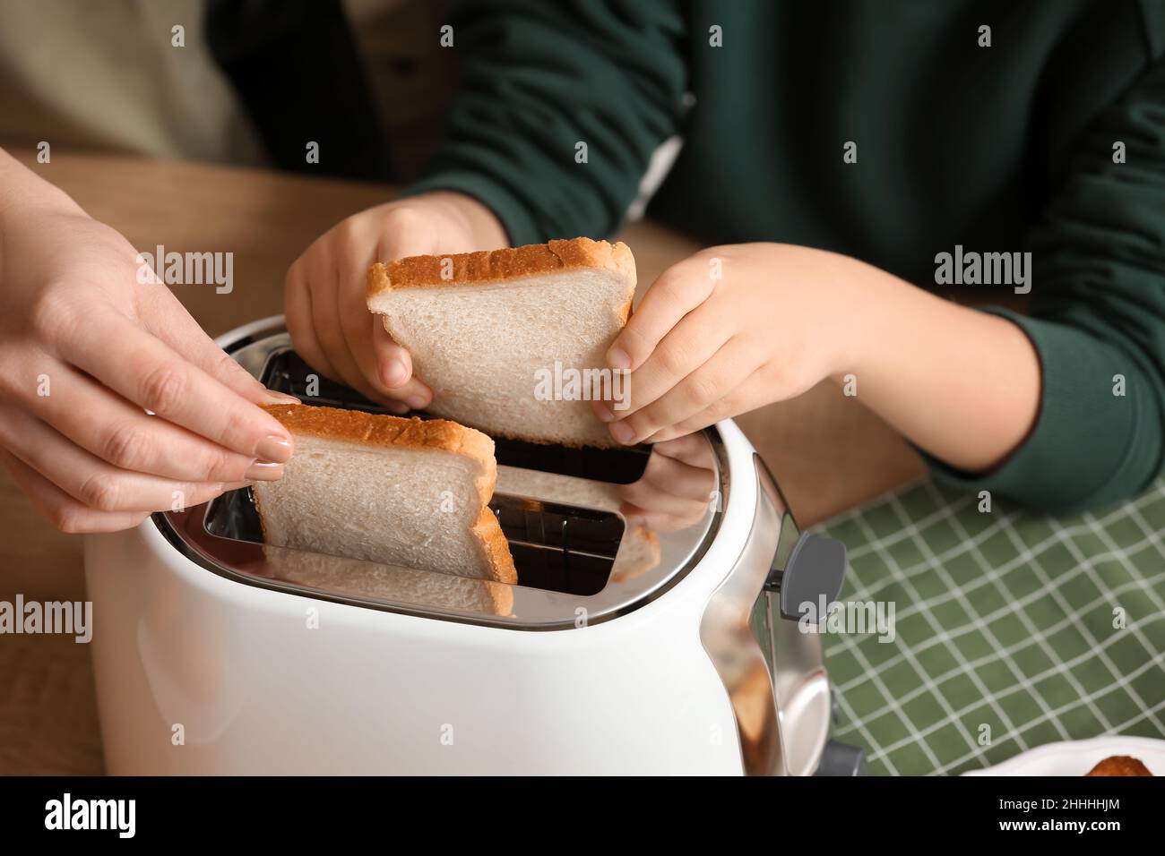 Little boy and his mother putting bread slices into toaster in kitchen ...