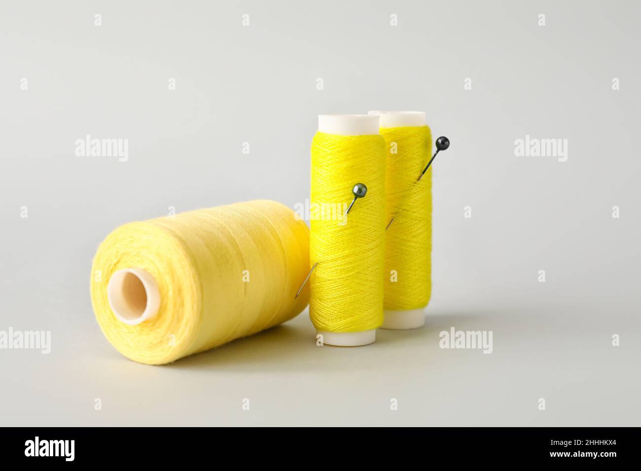 Yellow sewing thread spools with pins on light background Stock Photo ...