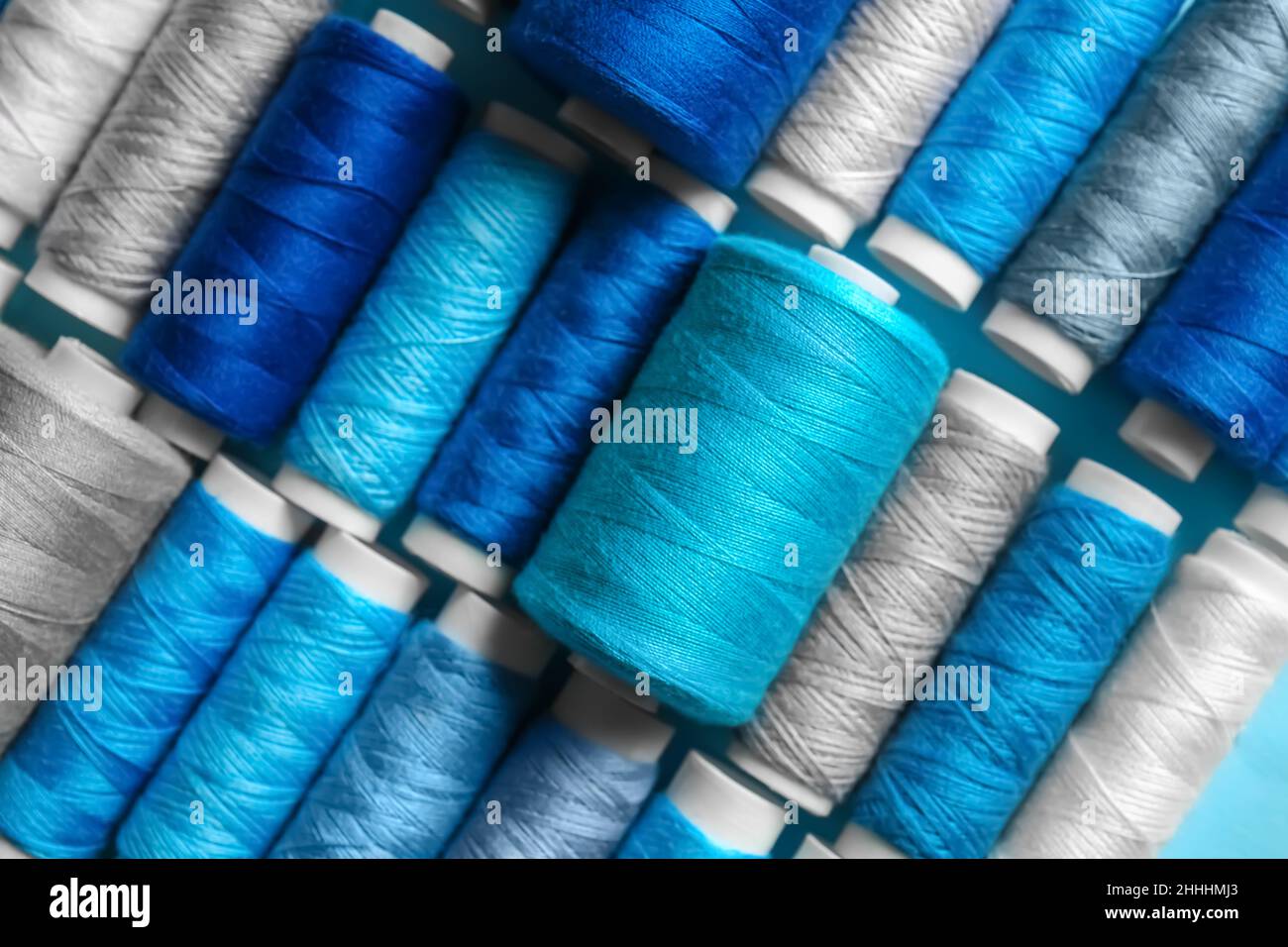 Closeup view of spools with grey and blue sewing threads as background ...