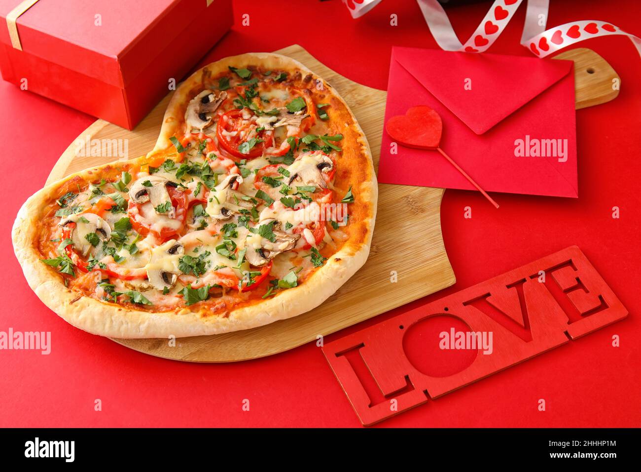 Wooden board with tasty heart-shaped pizza, decor and envelope on red ...