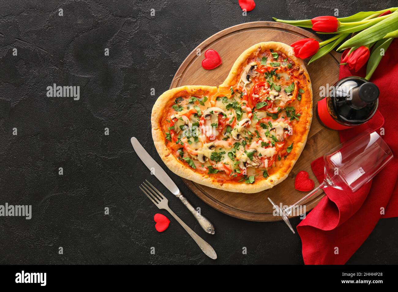 Wooden board with tasty heart-shaped pizza, tulip flowers and bottle of ...
