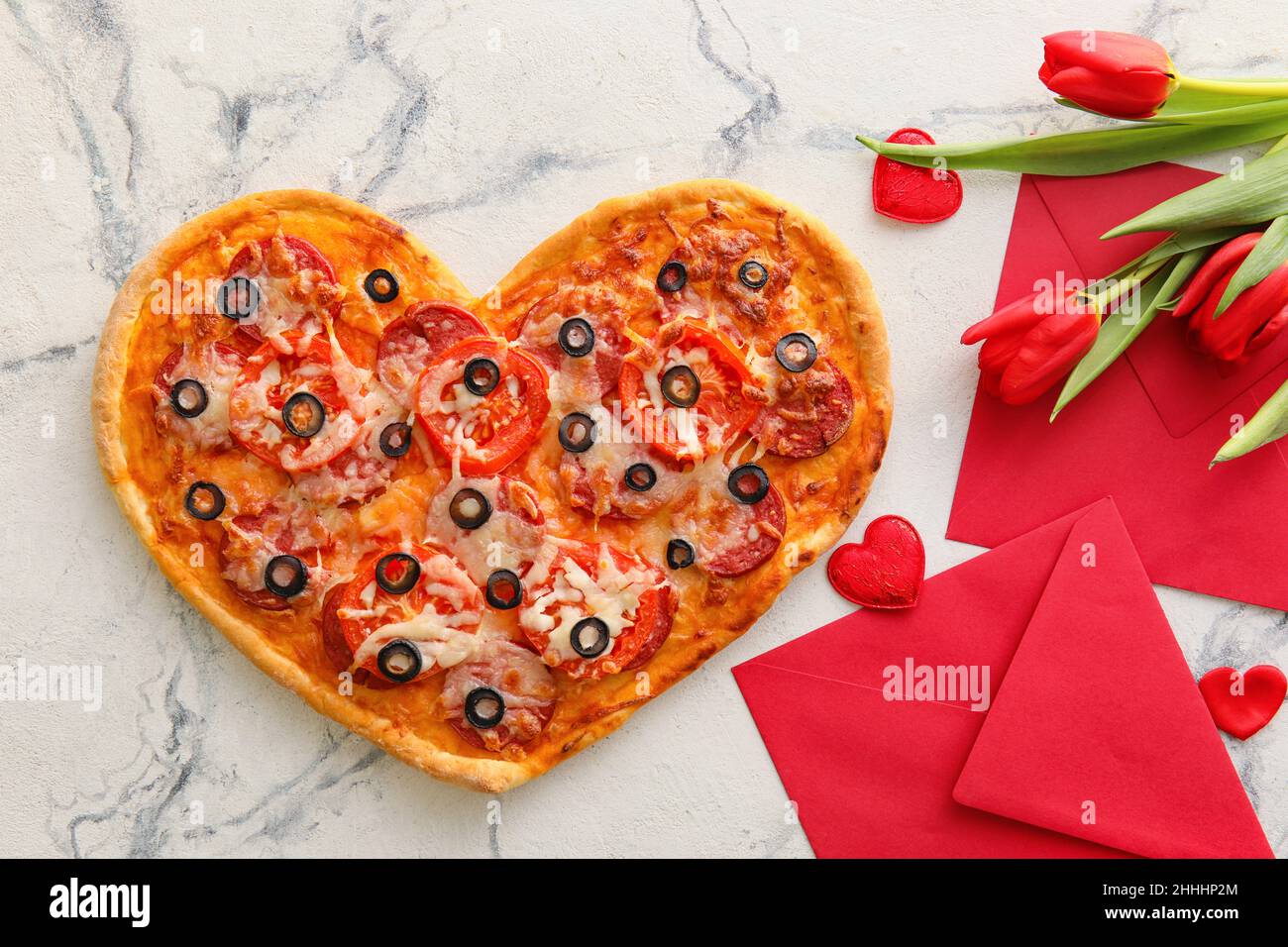 Tasty heart-shaped pizza, envelopes and tulip flowers on white marble ...