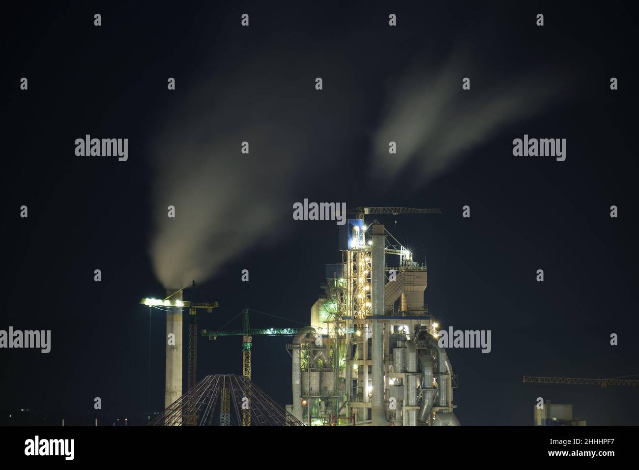 Illuminated cement plant with high factory structure and tower cranes ...