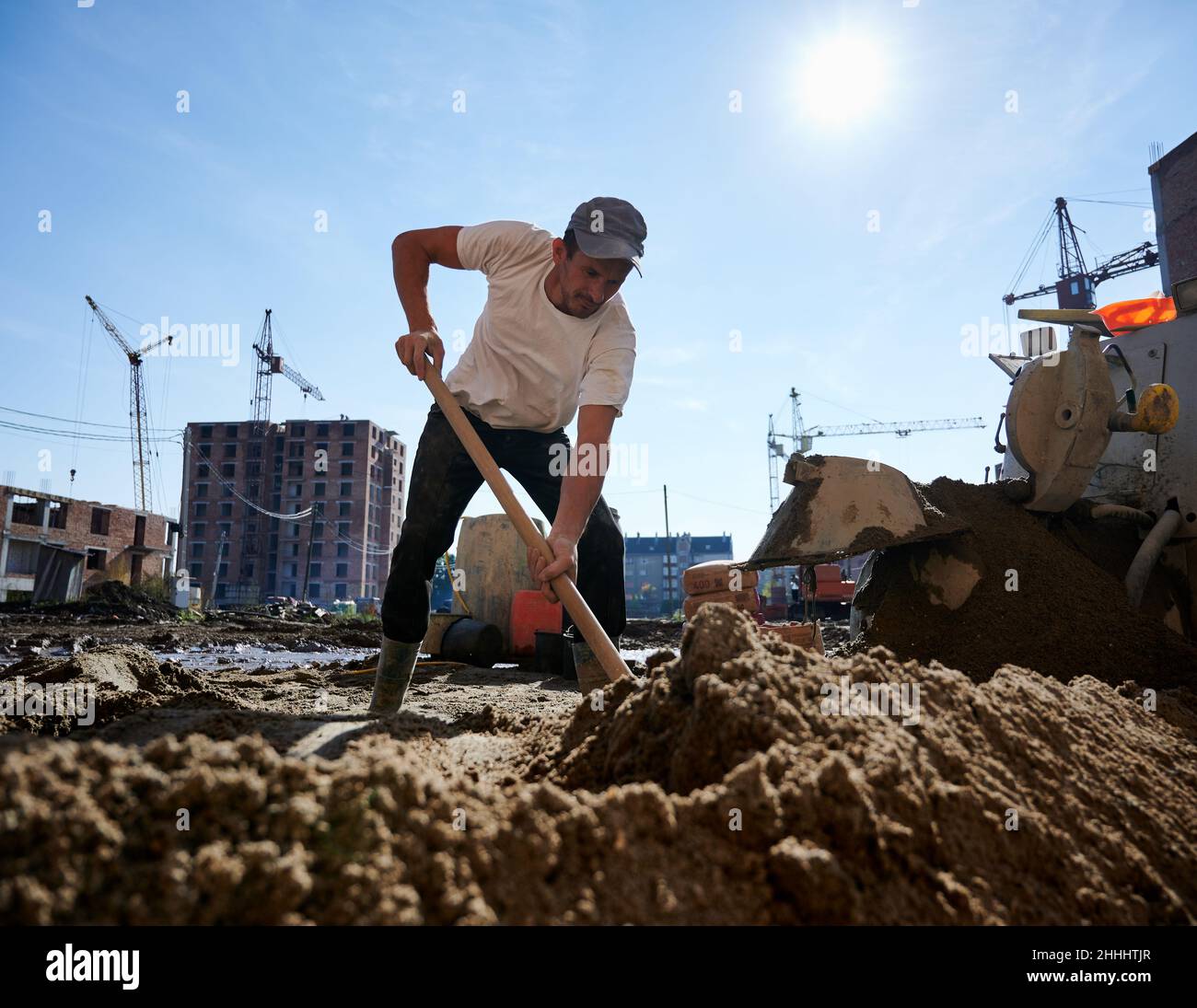 Workman laboring on street construction site and using shovel for ...