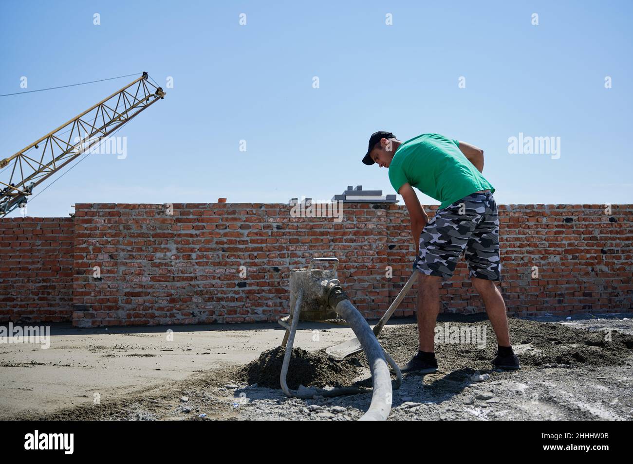 Full length of man in shorts shoveling sand-cement mix while working at ...
