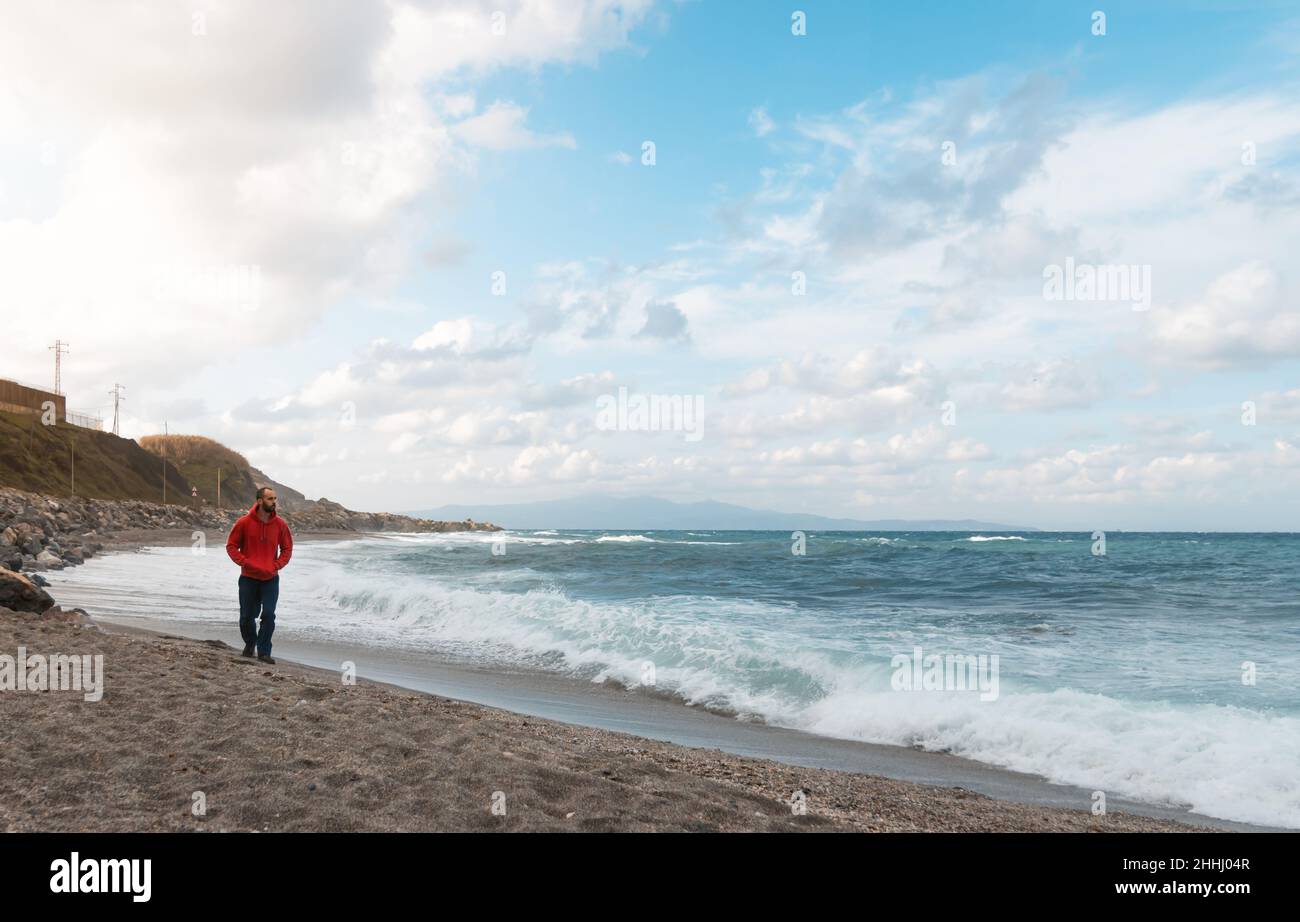 Man walking on a cloudy day on a beach with churning water Stock Photo ...
