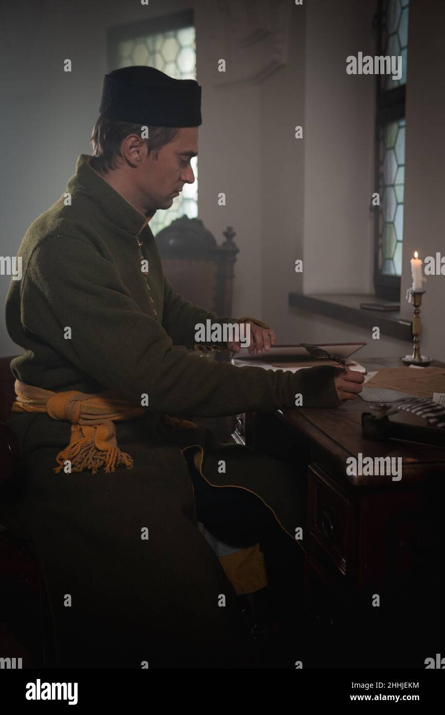 Portrait of a man in a medieval costume. A scribe writes on a red table ...