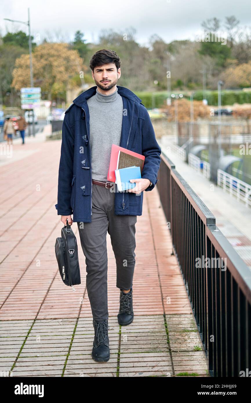 Full body of pensive male student carrying netbook case and books for ...