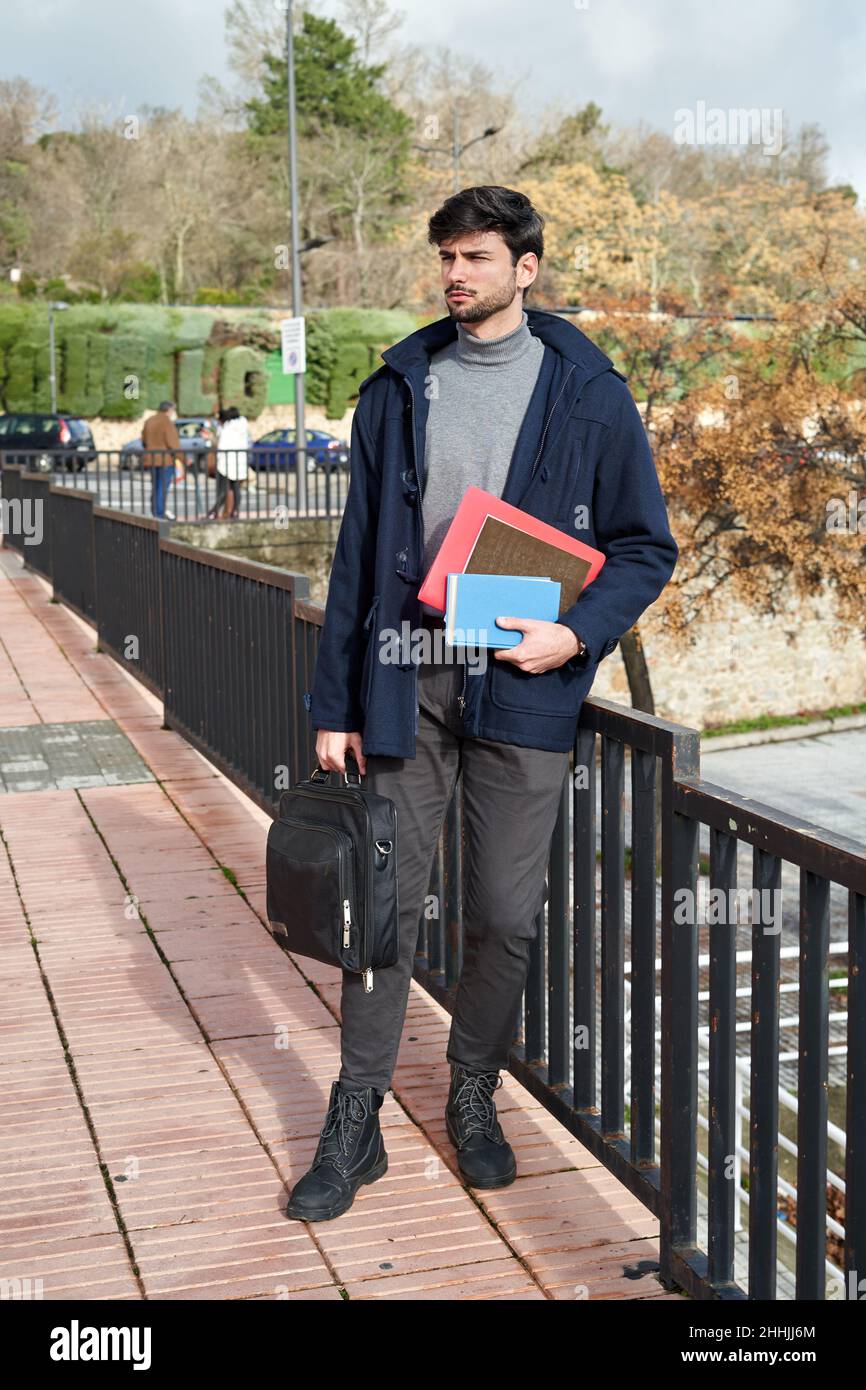 Full body of pensive male student carrying netbook case and books for ...