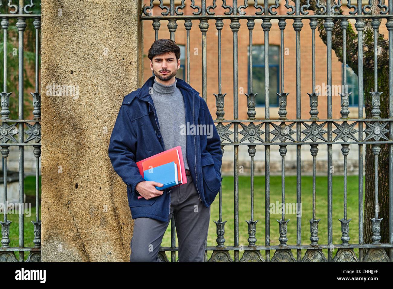 Serious male student in outerwear holding notepads and book for studies ...