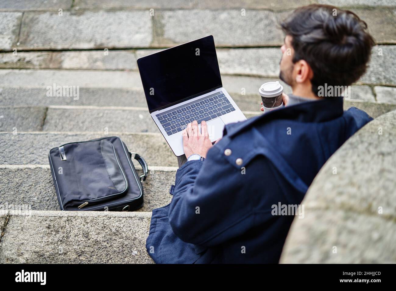 High angle back view of male student sitting on stone staircase and ...