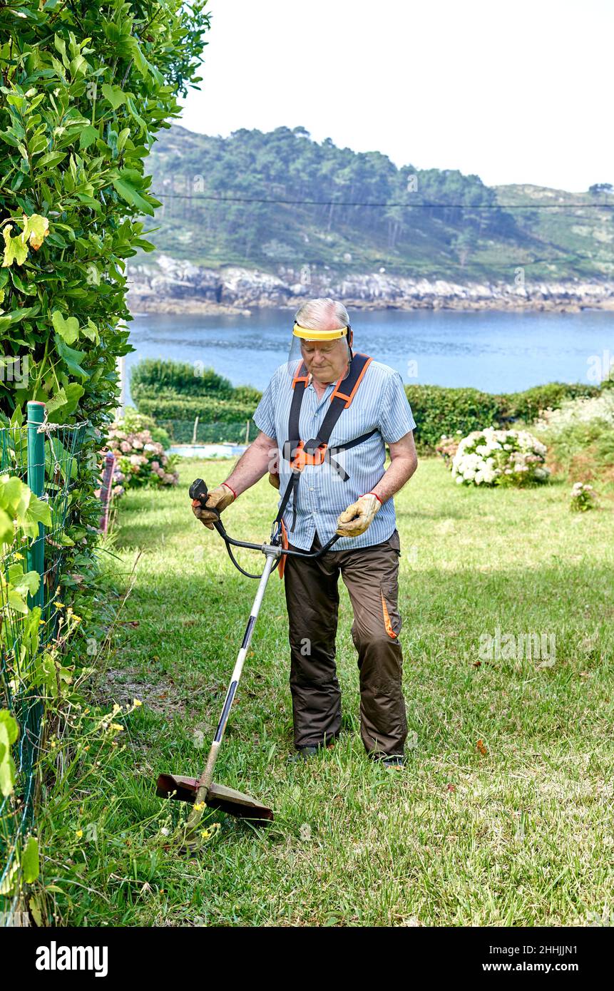Full body elderly man in protective shield mask mowing grass in ...