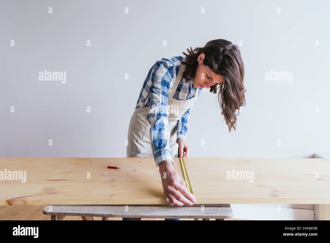 Concentrated female artisan in apron measuring wooden plank with ...
