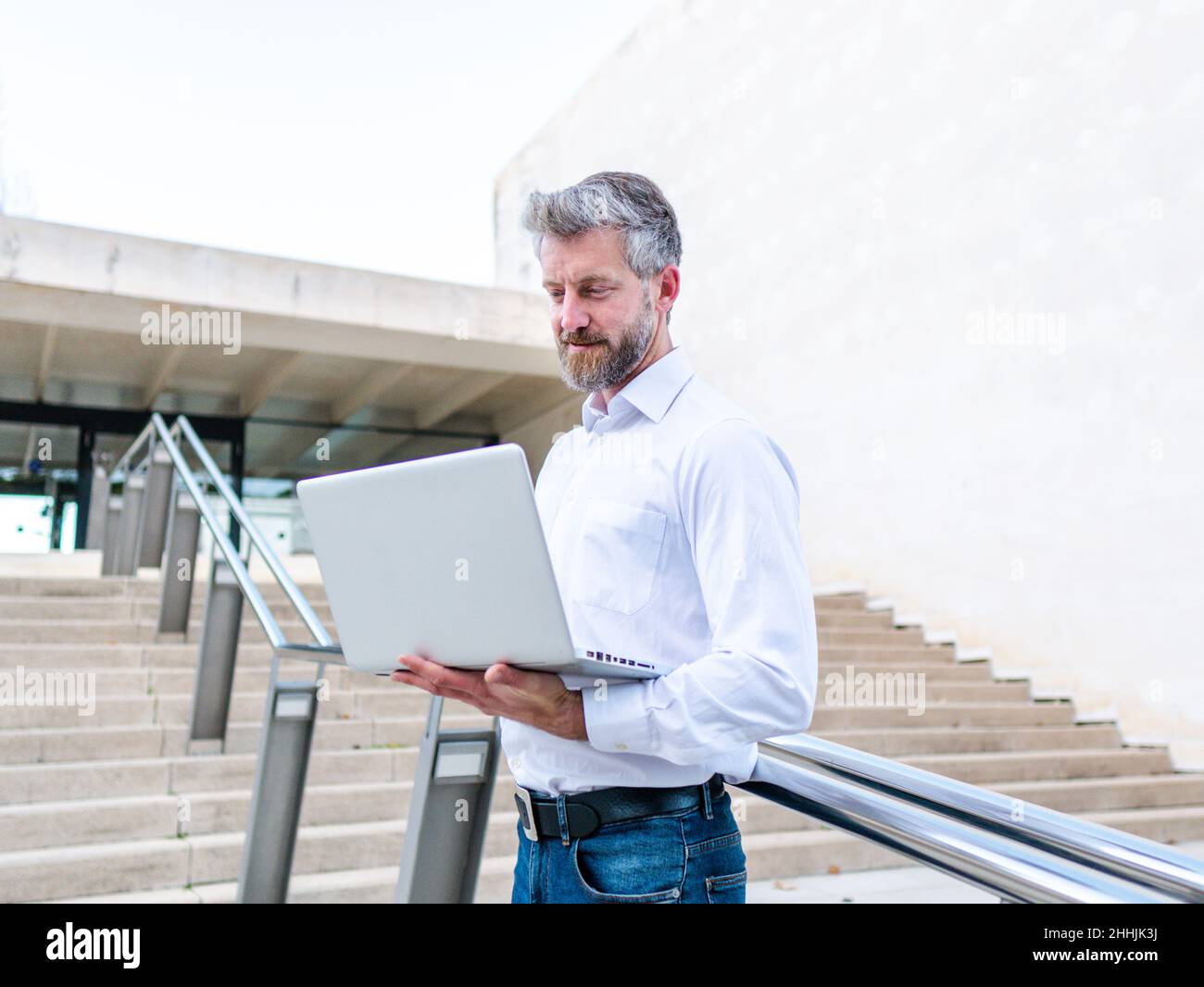 Confident male entrepreneur typing on modern netbook leaning on railing ...