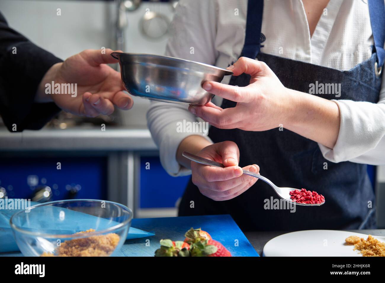 Crop female chef in blue apron taking bowl from male colleague while ...