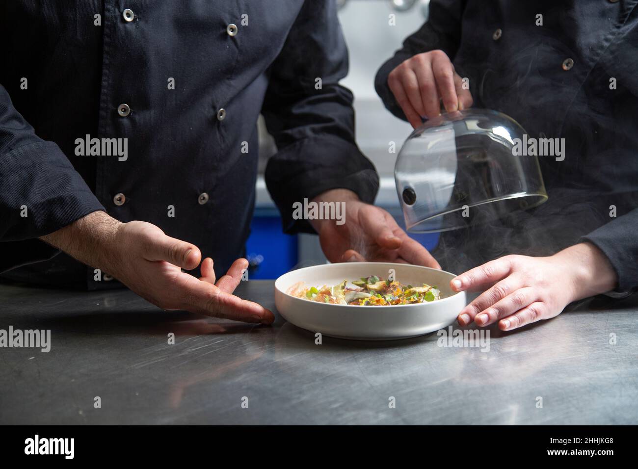Crop chefs in black uniform removing dome lid from tasty dish on table ...