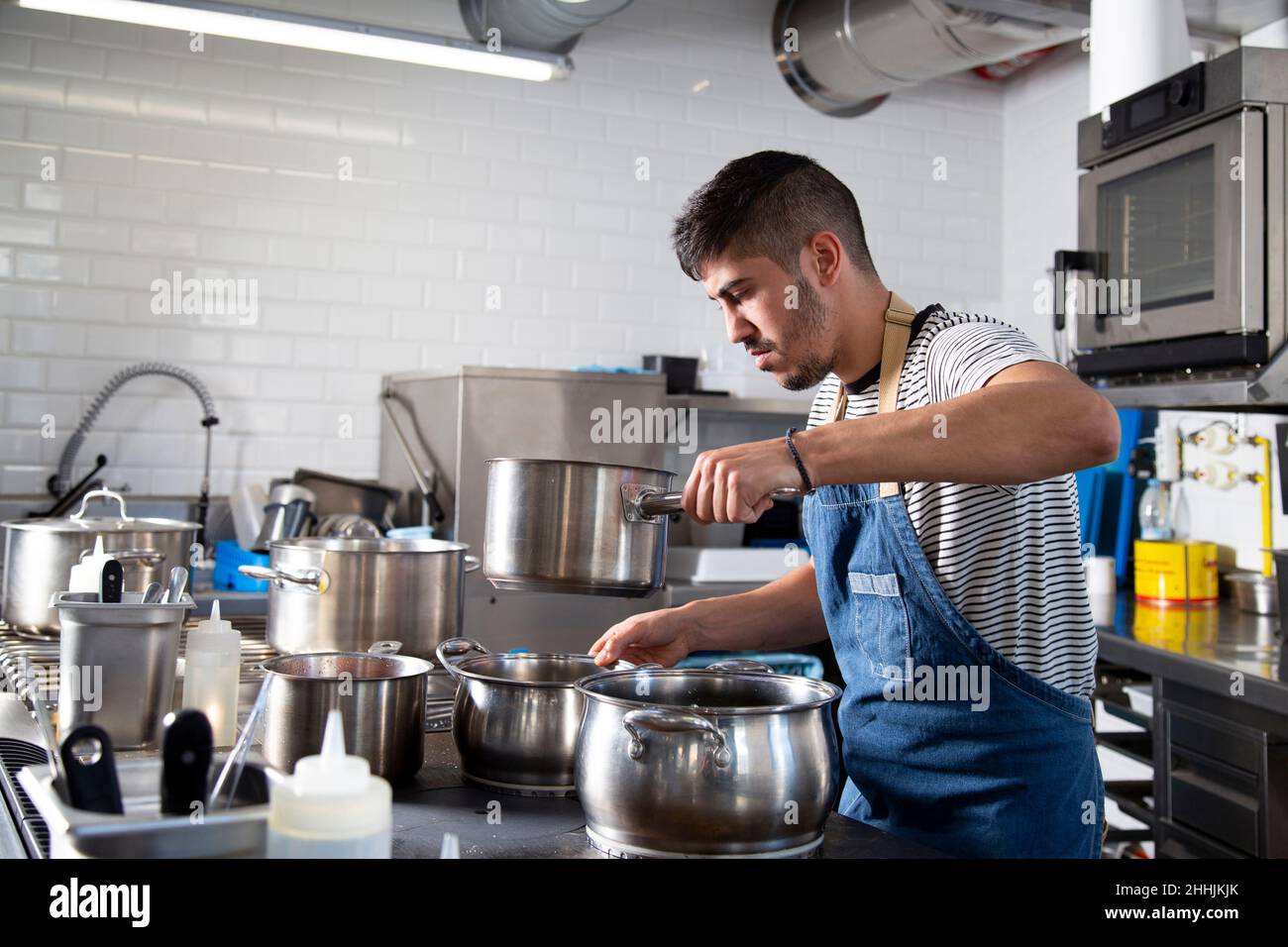 Concentrated young ethnic male cook with dark hair in t shirt and apron ...