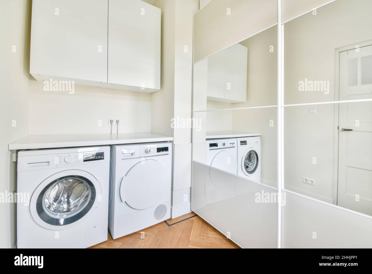 White modern washing machines placed at wall with cabinet in light ...