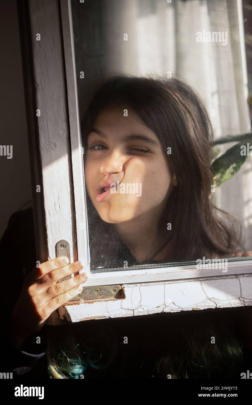 Funny ethnic girl pressing face against window and looking at camera ...