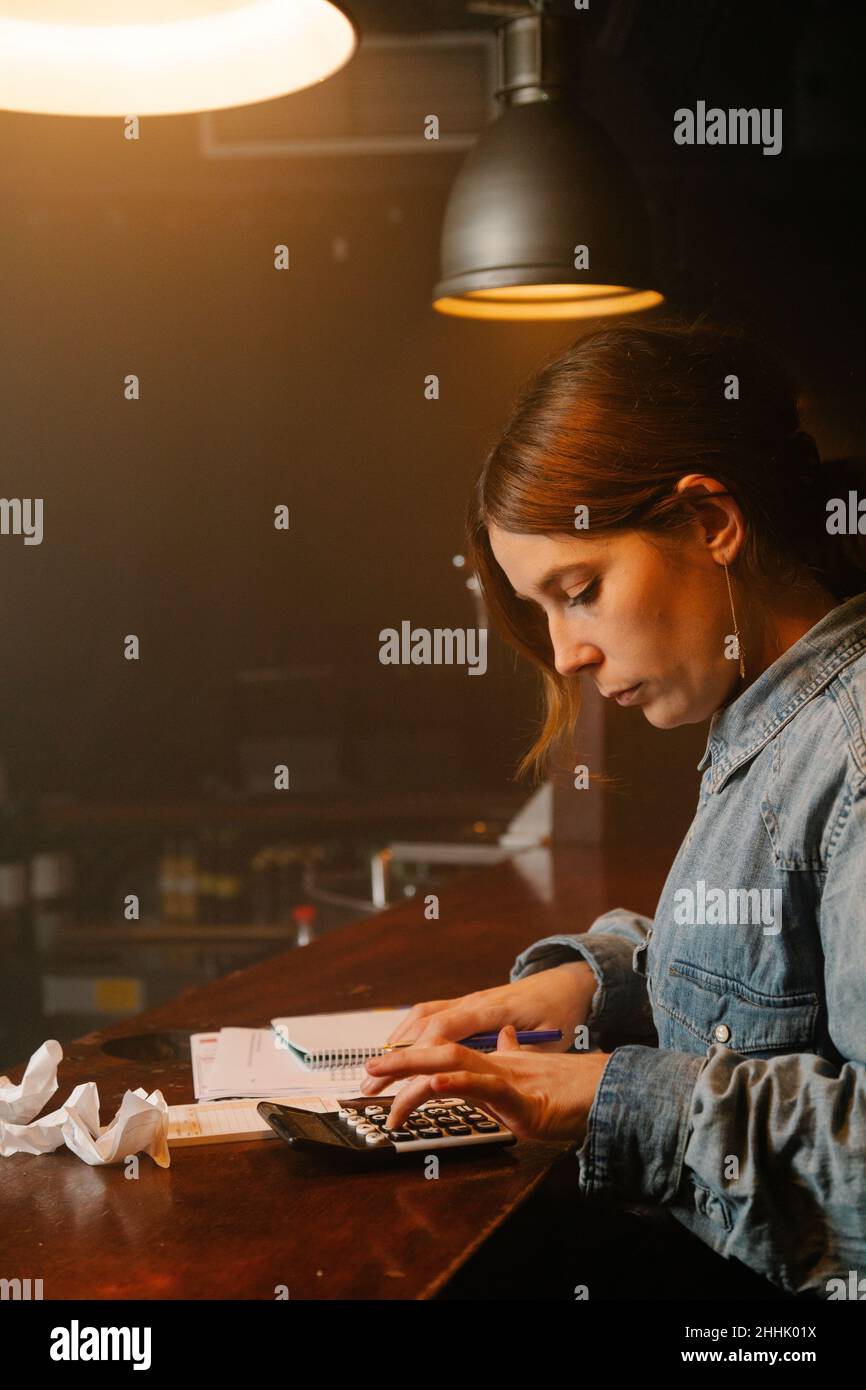 Side view of focused female worker using calculator to count income ...