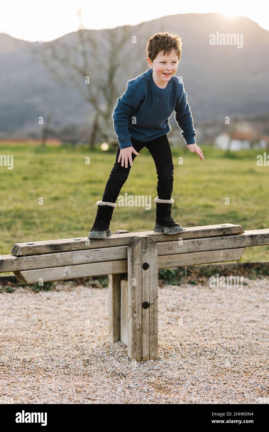 Full body of focused happy cute boy balancing and standing on wooden ...