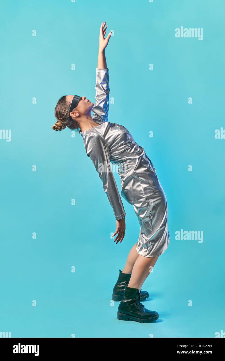 Side view of stylish young female in silver dress and VR headset while ...