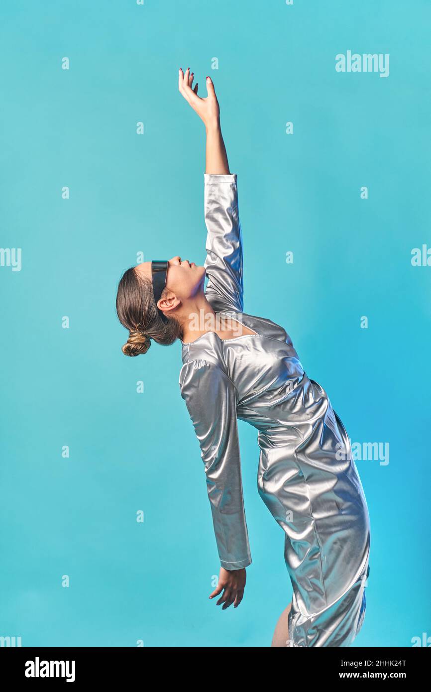 Side view of stylish young female in silver dress and VR headset while ...