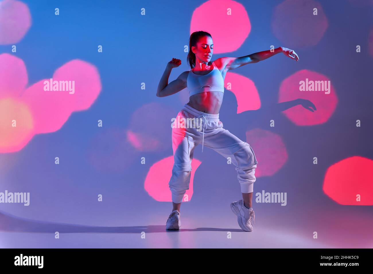 Full body of young female dancer in sportswear dancing in white studio ...