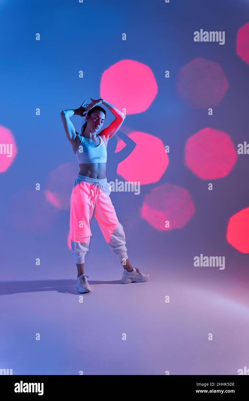 Full body of young female dancer in sportswear dancing in white studio ...