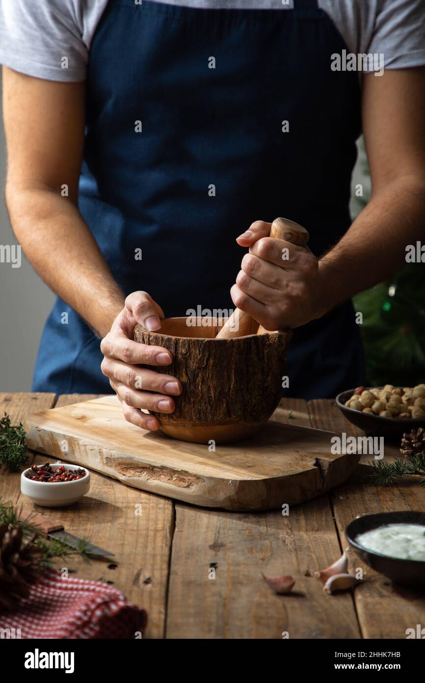 Crop unrecognizable male cook in apron grinding pepper in mortar with ...