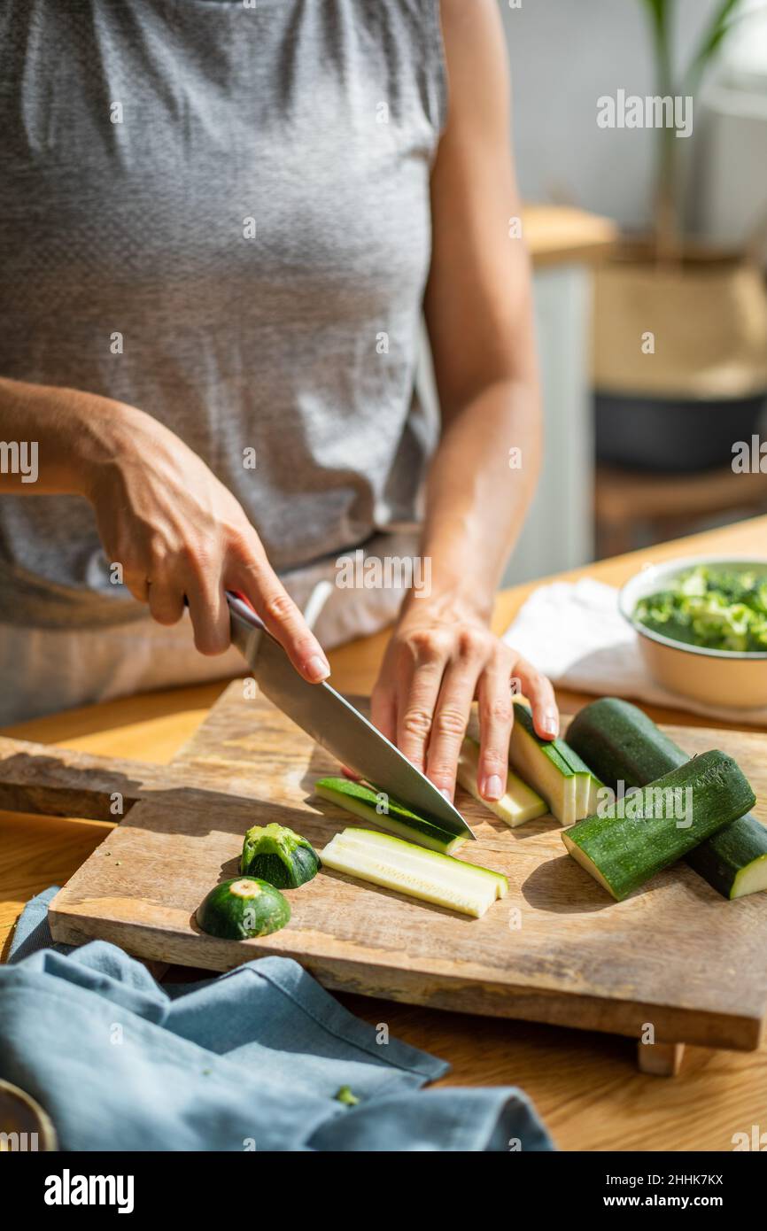 Crop anonymous female cook cutting fresh green cucumber with knife on ...