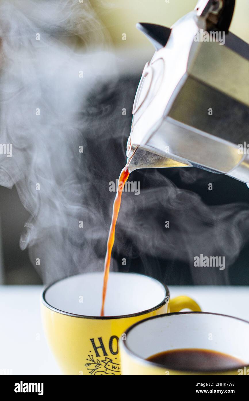 Freshly brewed steaming hot coffee pouring from metal moka pot into ...