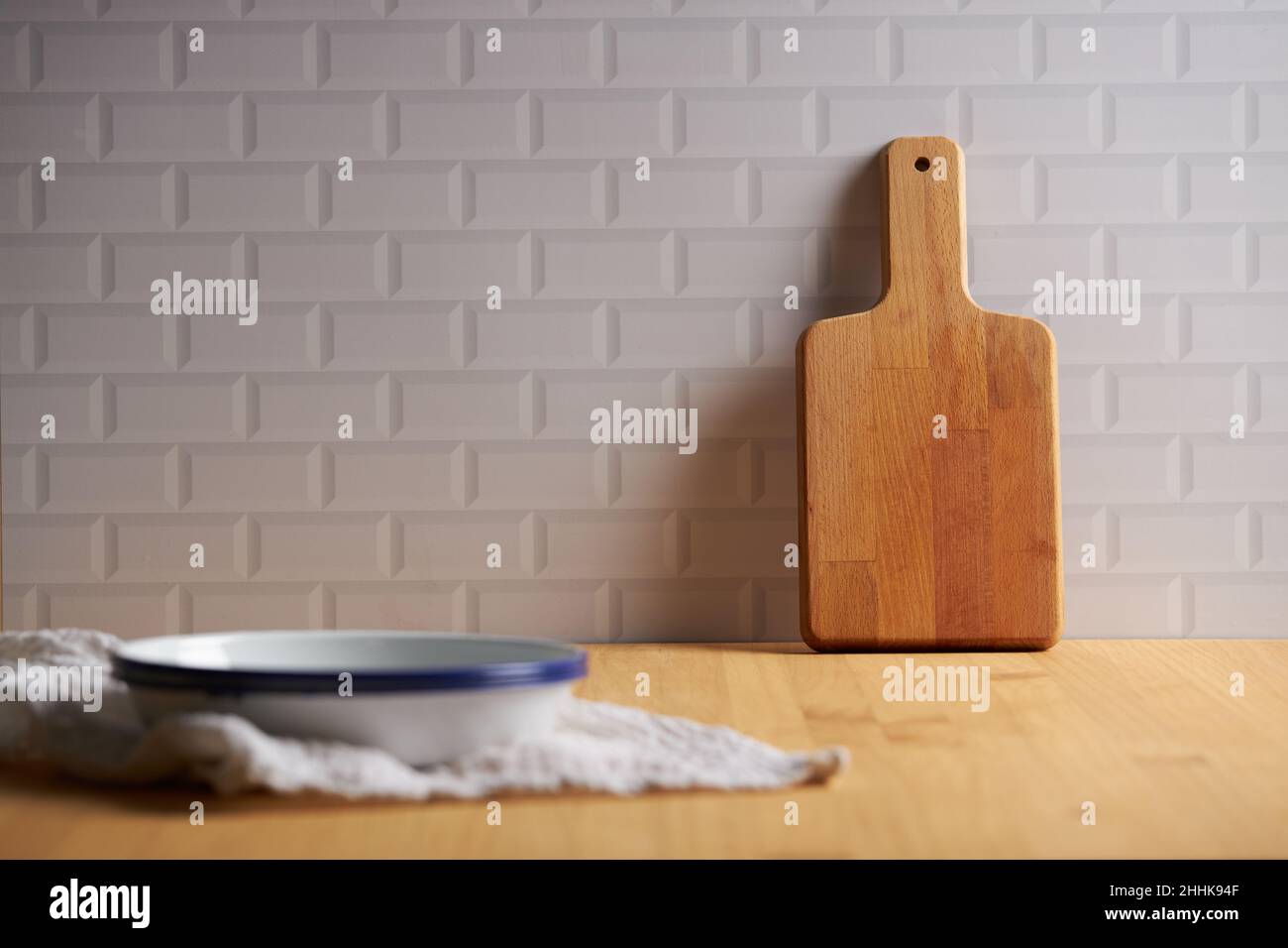 Wooden chopping board placed near wall on table with bowl in light ...
