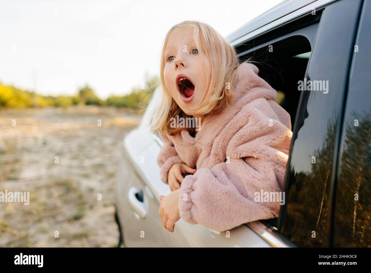 Astonished girl with blond hair looking out of automobile window with ...