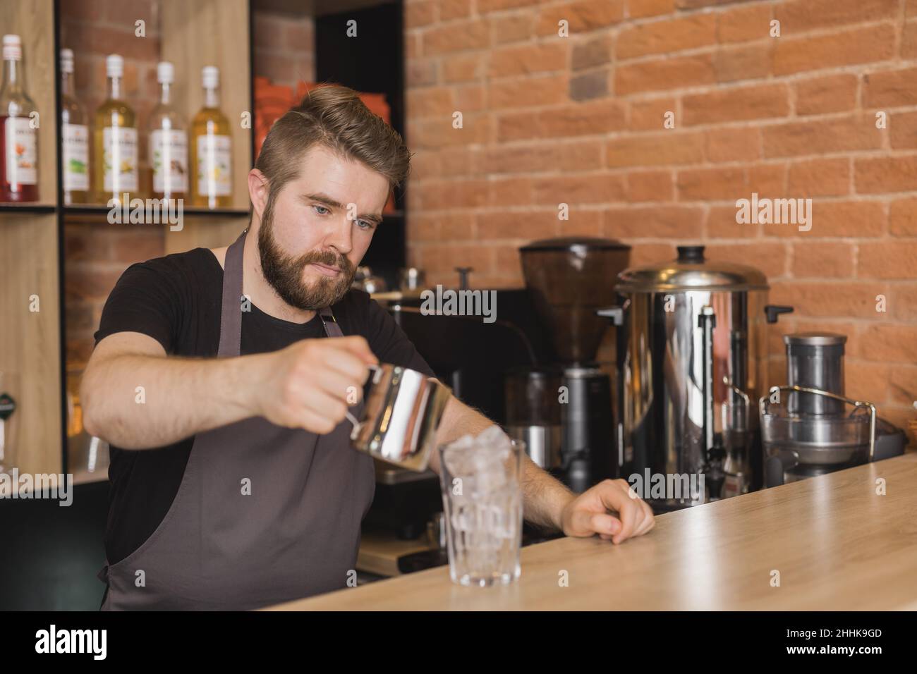 Serious bearded male barista in apron pouring ingredient from stainless ...