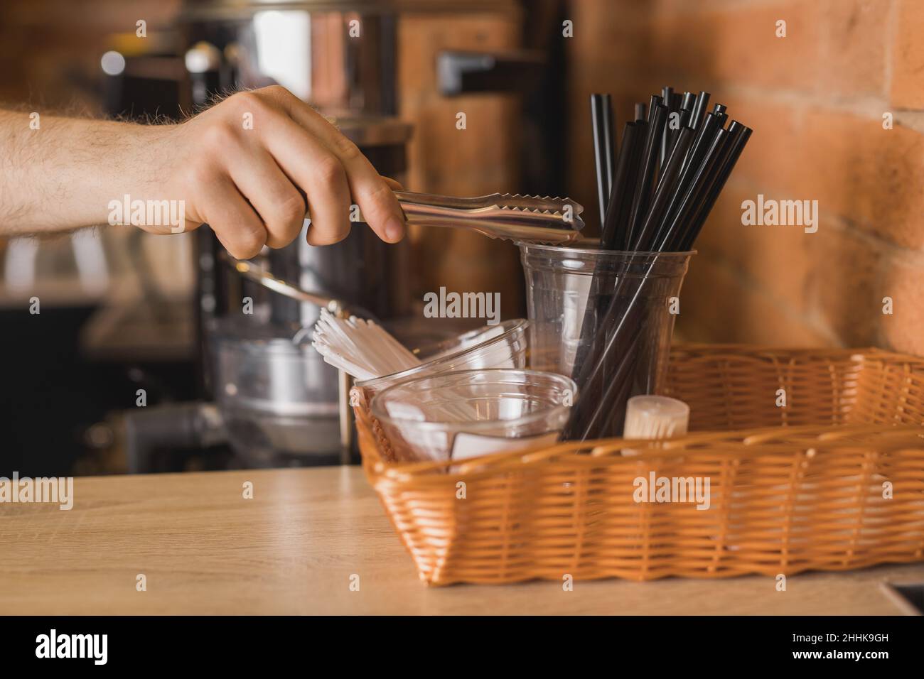 Crop anonymous male barista taking black plastic straw from cup using ...