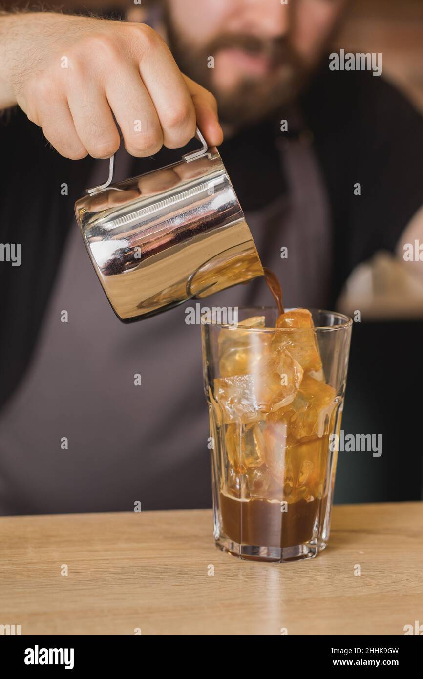 Crop bearded male barista in apron pouring ingredient from stainless ...