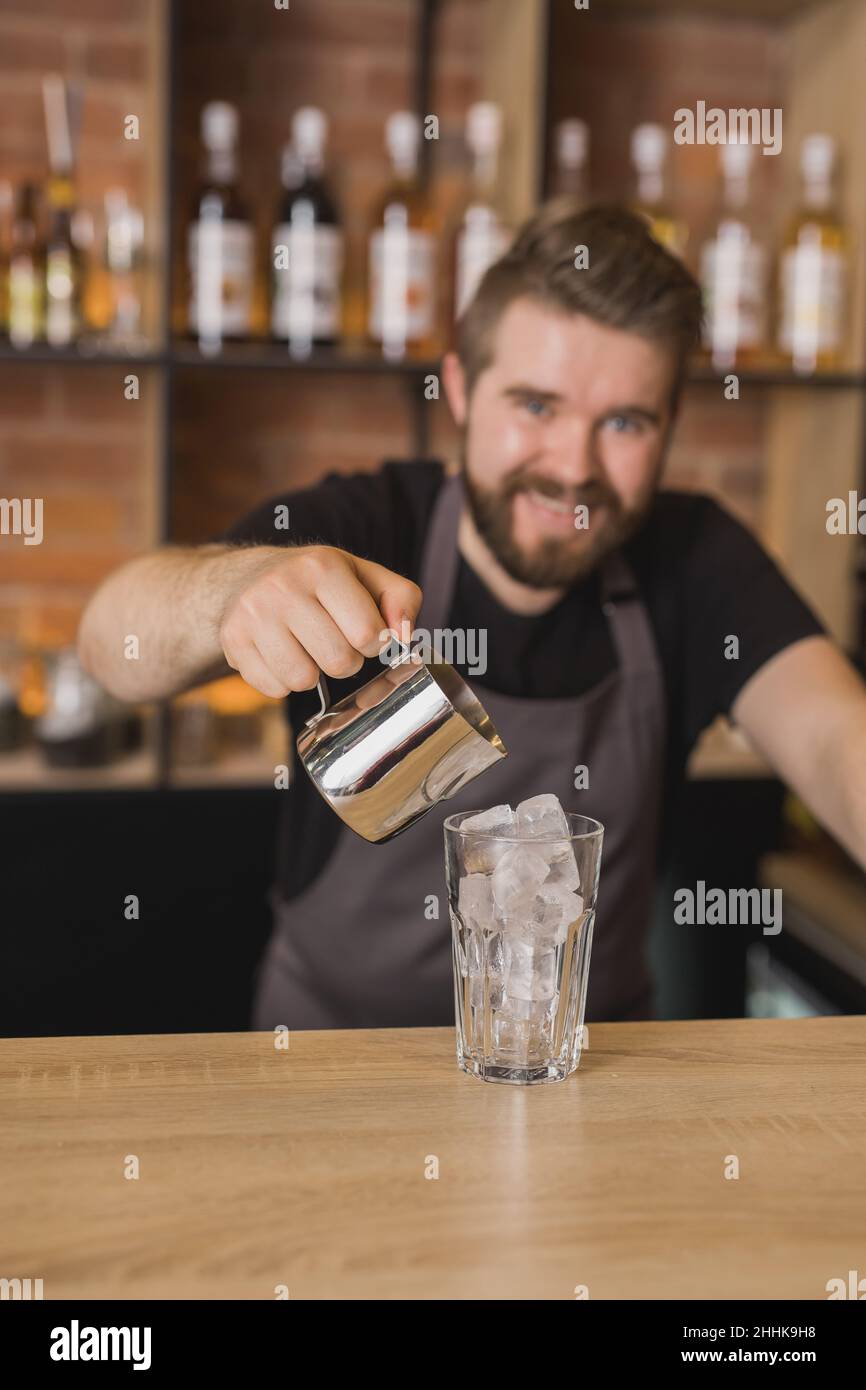 Cheerful bearded male barista in apron pouring ingredient from ...