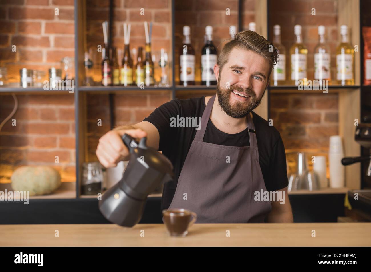 Cheerful male barista pouring hot aromatic Americano from stove top ...