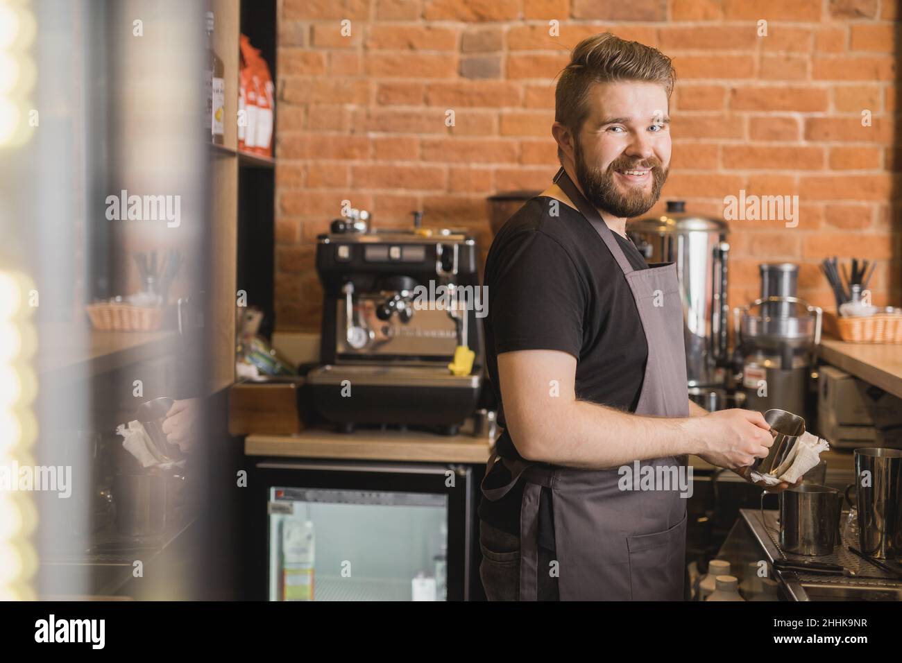 Side view of bearded male barista cleaning pitcher with napkin while ...